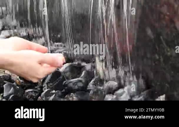 Womens hands under a stream of falling water in a fountain, a waterfall ...