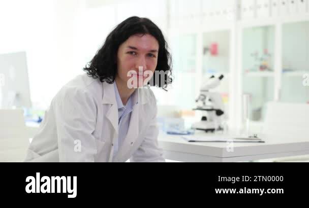 Young scientist with long hair sits at table in light laboratory. Male ...