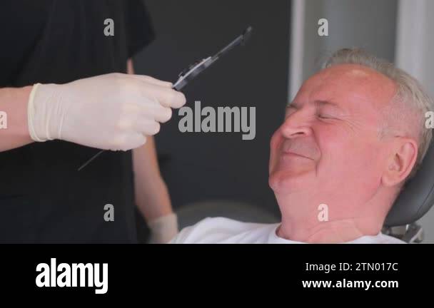 A surgeon is in front of an elderly man and makes marks on his face ...