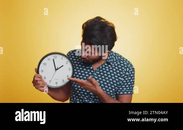 Young indian man with anxiety checking time on clock, running late to ...