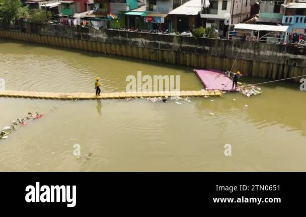 A polluted river with a garbage trap and workers cleaning up the river ...
