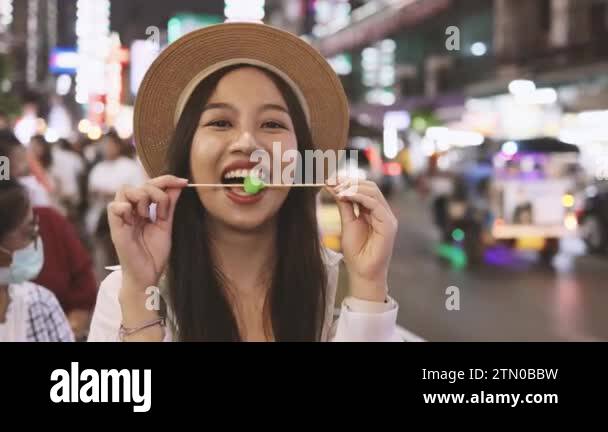 Asian woman enjoying and eating street food in night market with crowd of people at Yaowarat ...