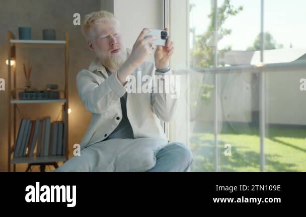 Albino man communicating via video link on smartphone, showing outdoor ...