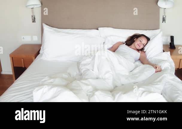 Young woman outstretching her arms sitting on the bed after good night ...