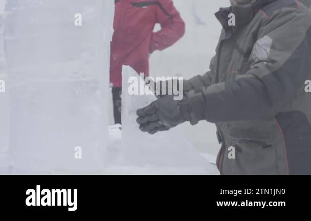 Worker using a chainsaw carving an ice sculpture. Men discuss work with ... Worker using a chainsaw carving an ice sculpture. Men discuss work with ...