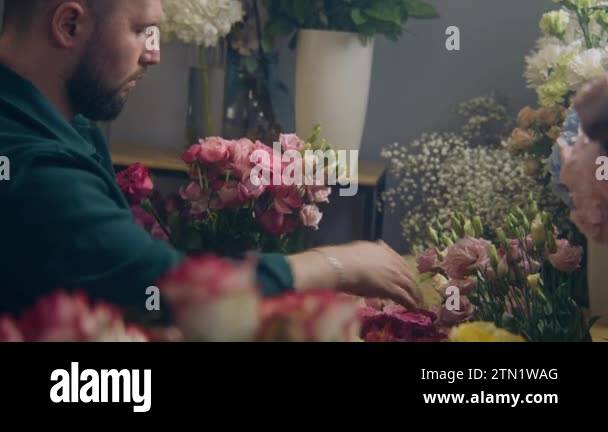 Male professional florist, owner, seller takes fresh spring flowers from vase and collects ...