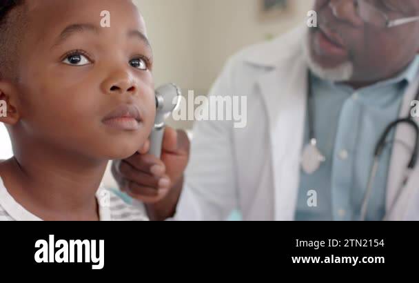 Senior african american male doctor checking ear of boy patient with ...