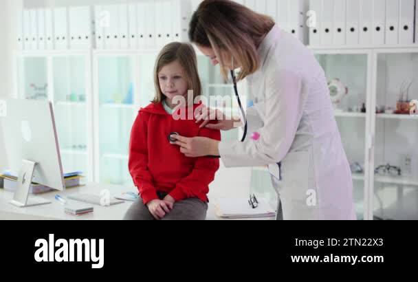 Woman doctor in work uniform examines little girl with stethoscope in ...