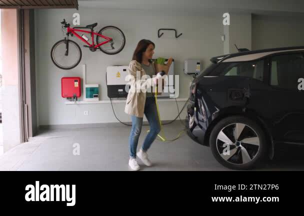 The woman parks in the garage, plugs a charger into the electric car ...
