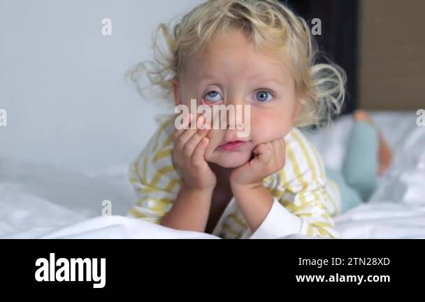 Cute funny child kid baby girl lying on bed and making faces, pulling ...