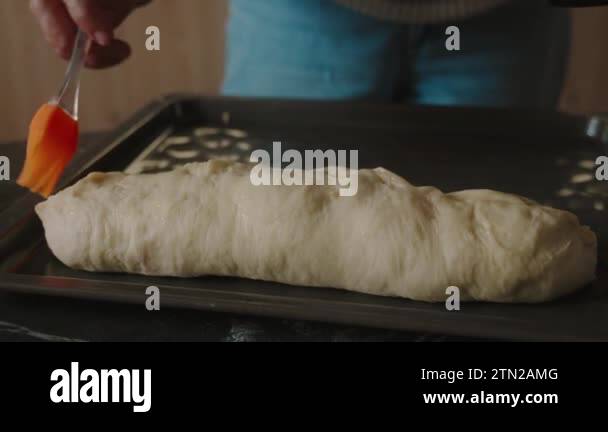 Senior womans hands greasing raw dough on a metal baking sheet with a ...