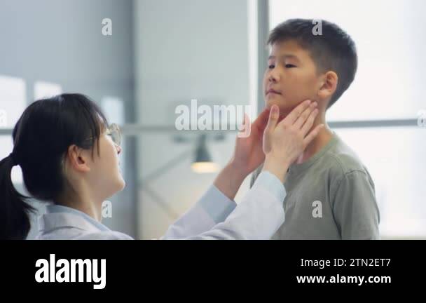 Asian female doctor touching lymph nodes on neck of tween boy during ...
