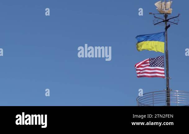 The flags of Ukraine and the USA flutter on a flagpole against a blue ...