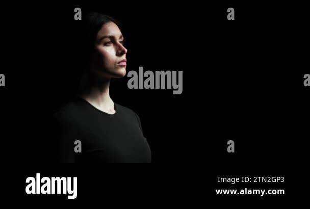 Woman of dramatic appearance stands in the dark on a black background ...