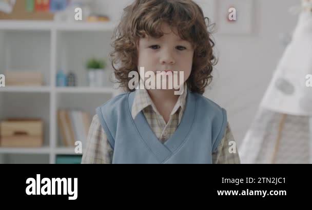 Calm and pensive little boy standing in nursery room with sad face feeling lonely at home ...