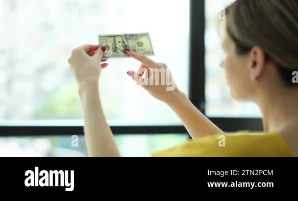 Woman checks watermarks on money dollars in front of window. Recognize ...