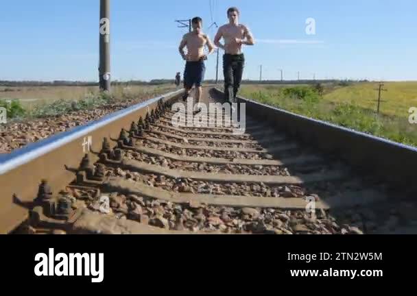 Two men are running between rails on railroad tracks. Sprinting runner ...
