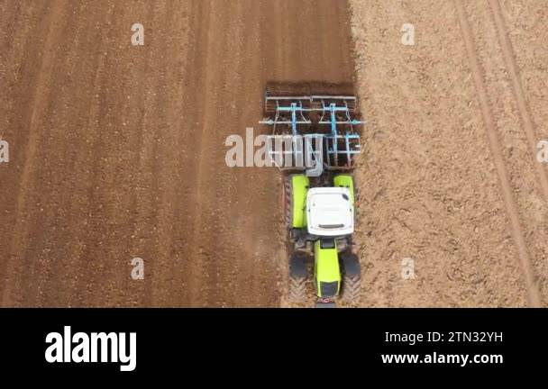 Tractor with harrow system plowing ground on cultivated farm field ...
