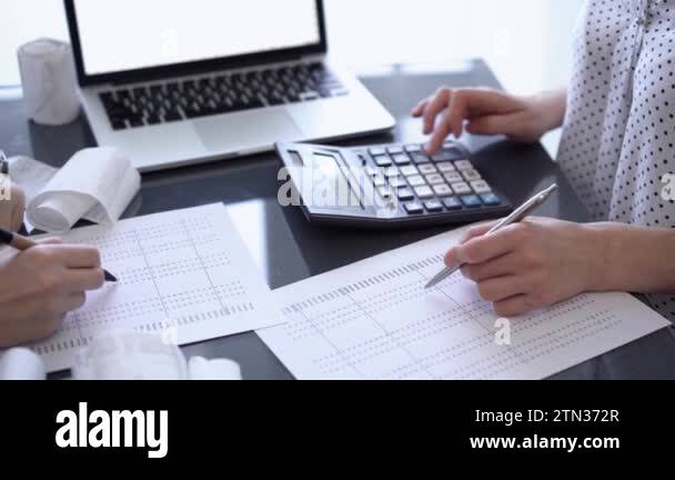 Two accountants use a calculator and laptop computer for counting taxes ...