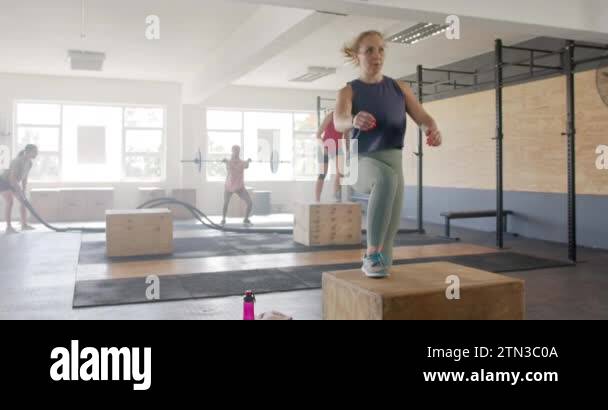 Unaltered diverse women jumping on boxes and training at fitness class ...
