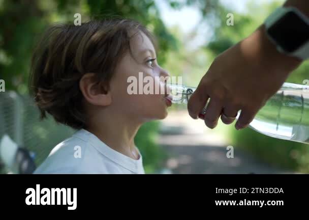 Little boy drinking water from glass bottle outside at park. Child hydrating drinks refreshing ...