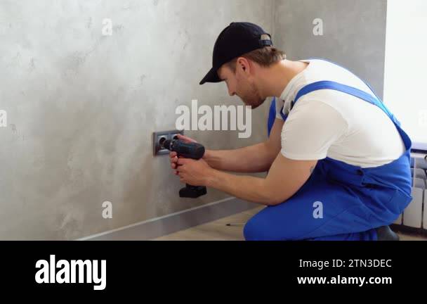 A young electrician installing an electrical socket in a new house ...