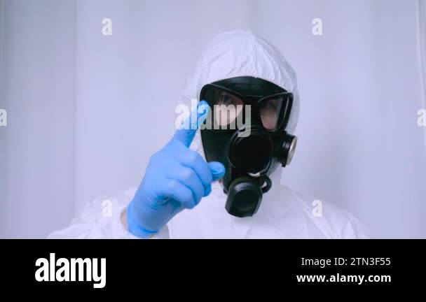 A man in a chemical protective suit with a gas mask pointing with his ...
