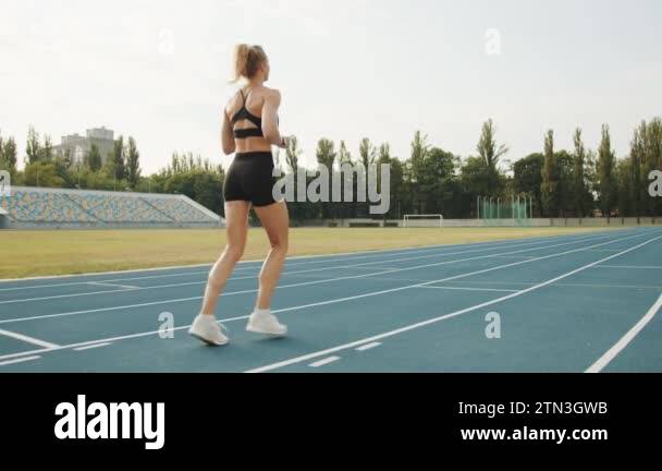Back view of sporty tall blonde running on athletics track in the ...