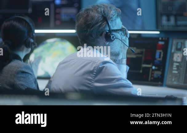 Diverse flight control workers sit in front of computers, monitor space ...