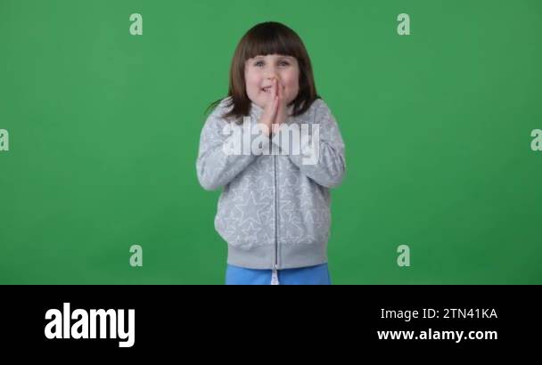 Cheerful young girl standing on a green screen, clapping her hands and ...