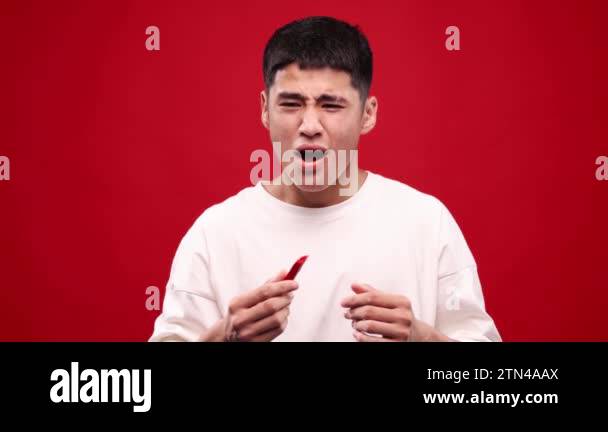 Burning mouth. Young asian man eating red hot chilli peppers against ...