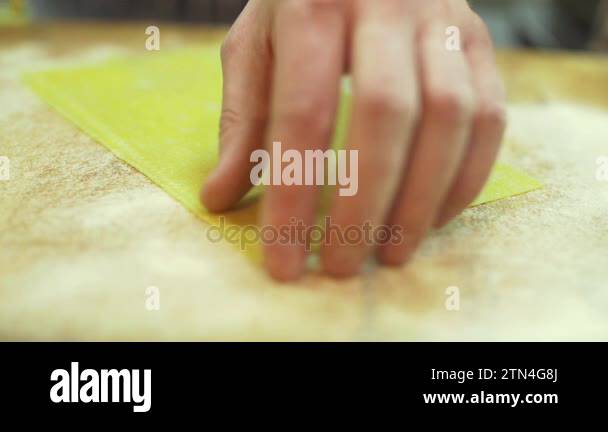 Mens Chef hands cut a thin layer of dough to use a roller professional ...
