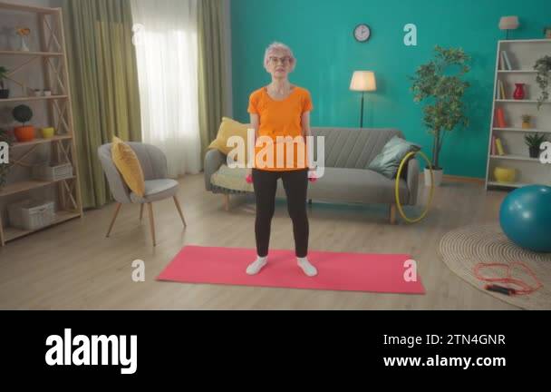 Grayhaired elderly woman doing fitness with dumbbells at home. A mature ...