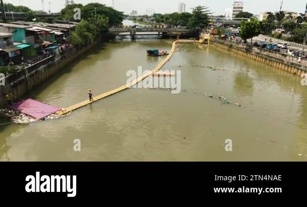 A polluted river with a garbage trap and workers cleaning up the river ...