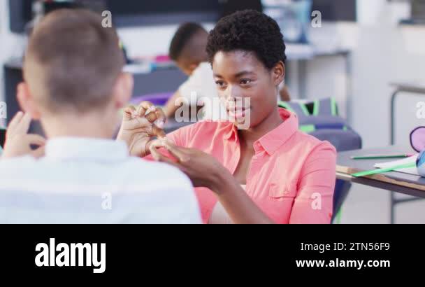 Diverse female teacher and happy schoolchildren at desks learning sign ...