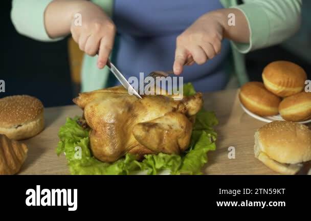 Fat woman carving roughly roast chicken with fork and knife, eating ...