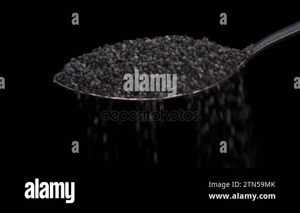 Heap poppy seeds falling from the iron spoon, black background, slow ...