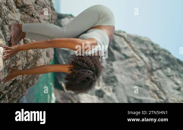 African american sporty girl practicing yoga pose standing on cliff ...