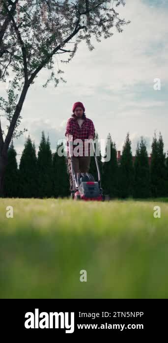 Vertical view of lawn-mover worker cutting green grass garden. Young ...