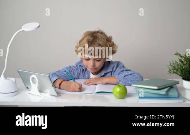 Elementary school student boy or girl writing letters, studying at desk ...
