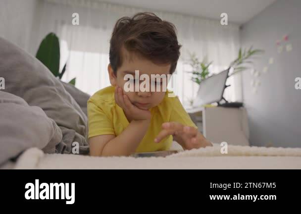 Adorable little child lying on sofa touching mobile phone screen while ...