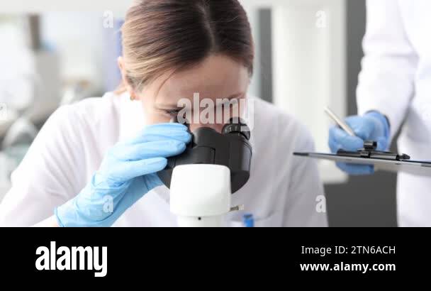 Woman biologist showing assistant sample in microscope 4k movie. Dna ...