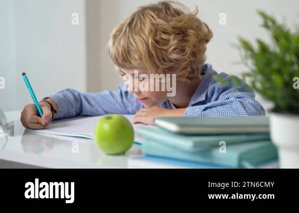 Elementary school student boy or girl writing letters, studying at desk ...