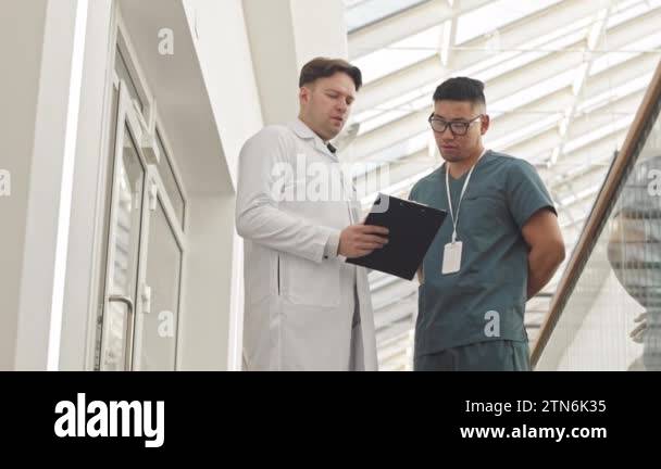 Low angle slowmo of Caucasian doctor in lab coat and his Asian ...