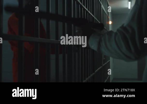 Prison guard with police baton watches criminals in prison cells ...