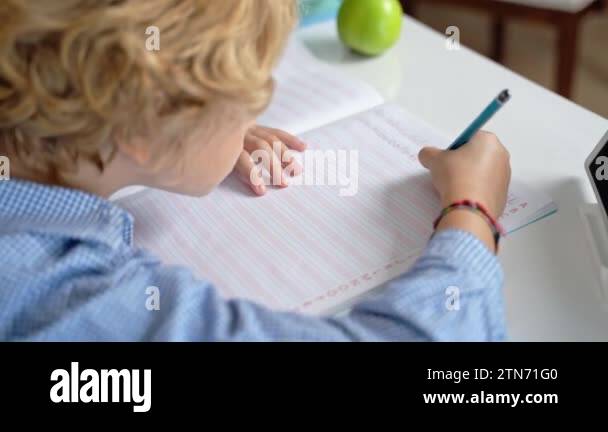 Elementary school student boy or girl writing letters, studying at desk ...