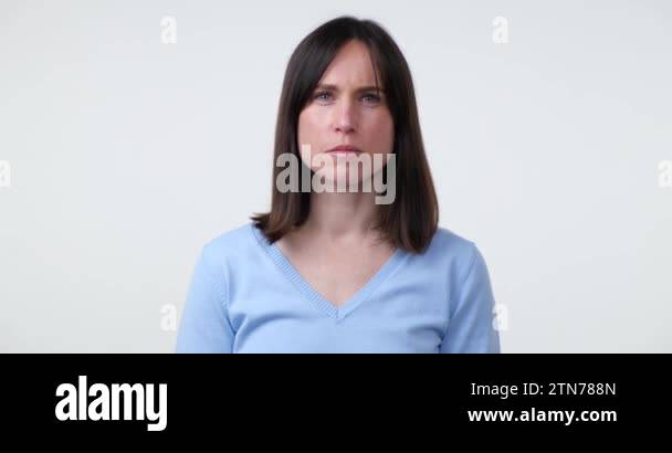 A Caucasian woman standing on a white background stares intently at the ...