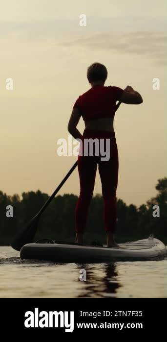 Vertical Screen: Woman in red sportswear paddling on SUP board, ripples ...