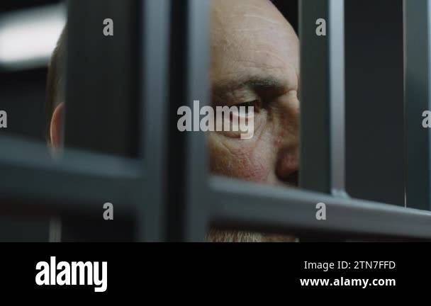 Face close up of depressed elderly prisoner standing behind metal bars ...