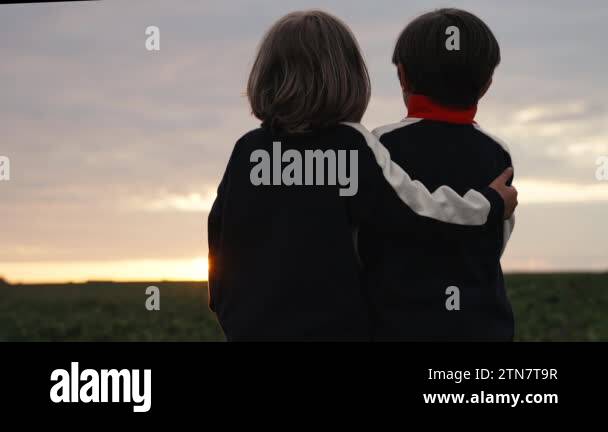 Hugging children watching sunset, look at horizon on meadow nature ...